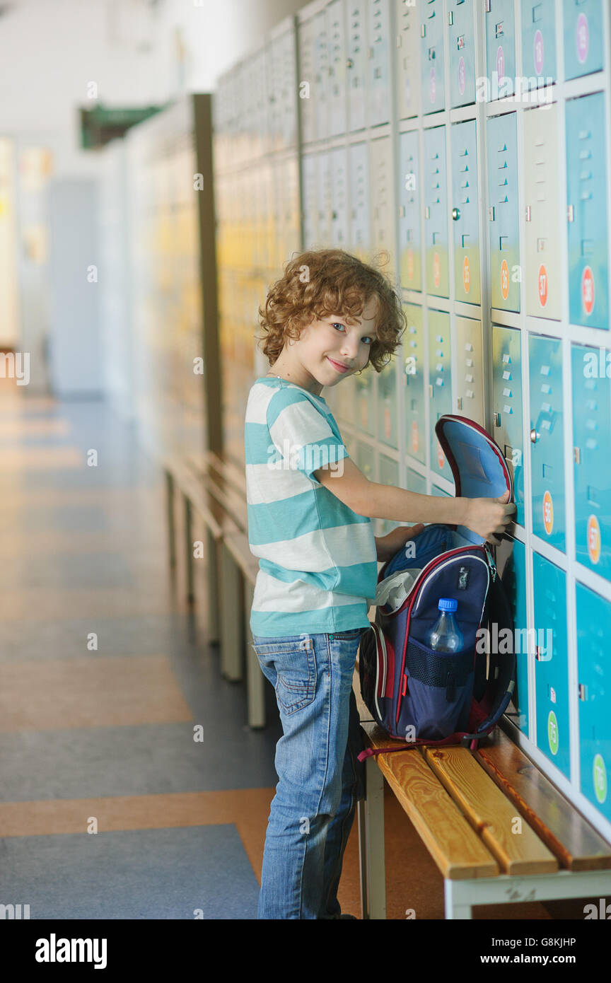 Little schoolboy standing near lockers in school hallway. He put the ...