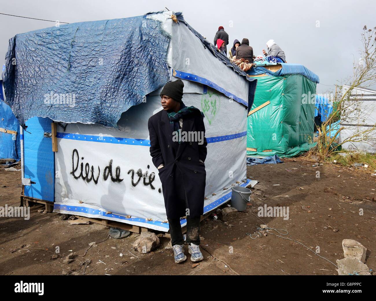 A migrant in the Calais migrant camp known as the Jungle watches as a ...