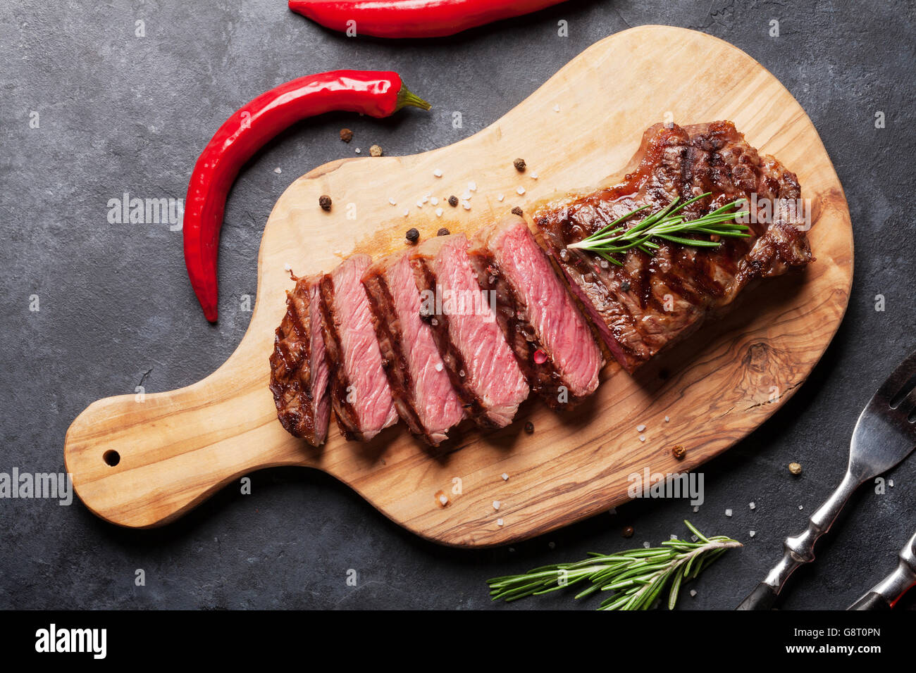 Grilled sliced beef steak on cutting board over stone table. Top view ...