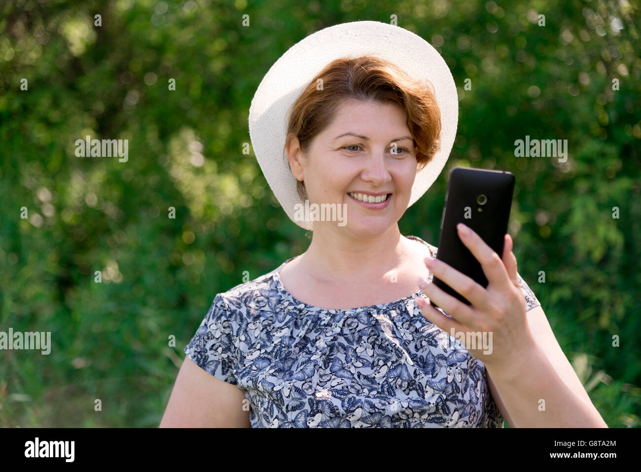 woman in hat looks at cell phone outside Stock Photo - Alamy