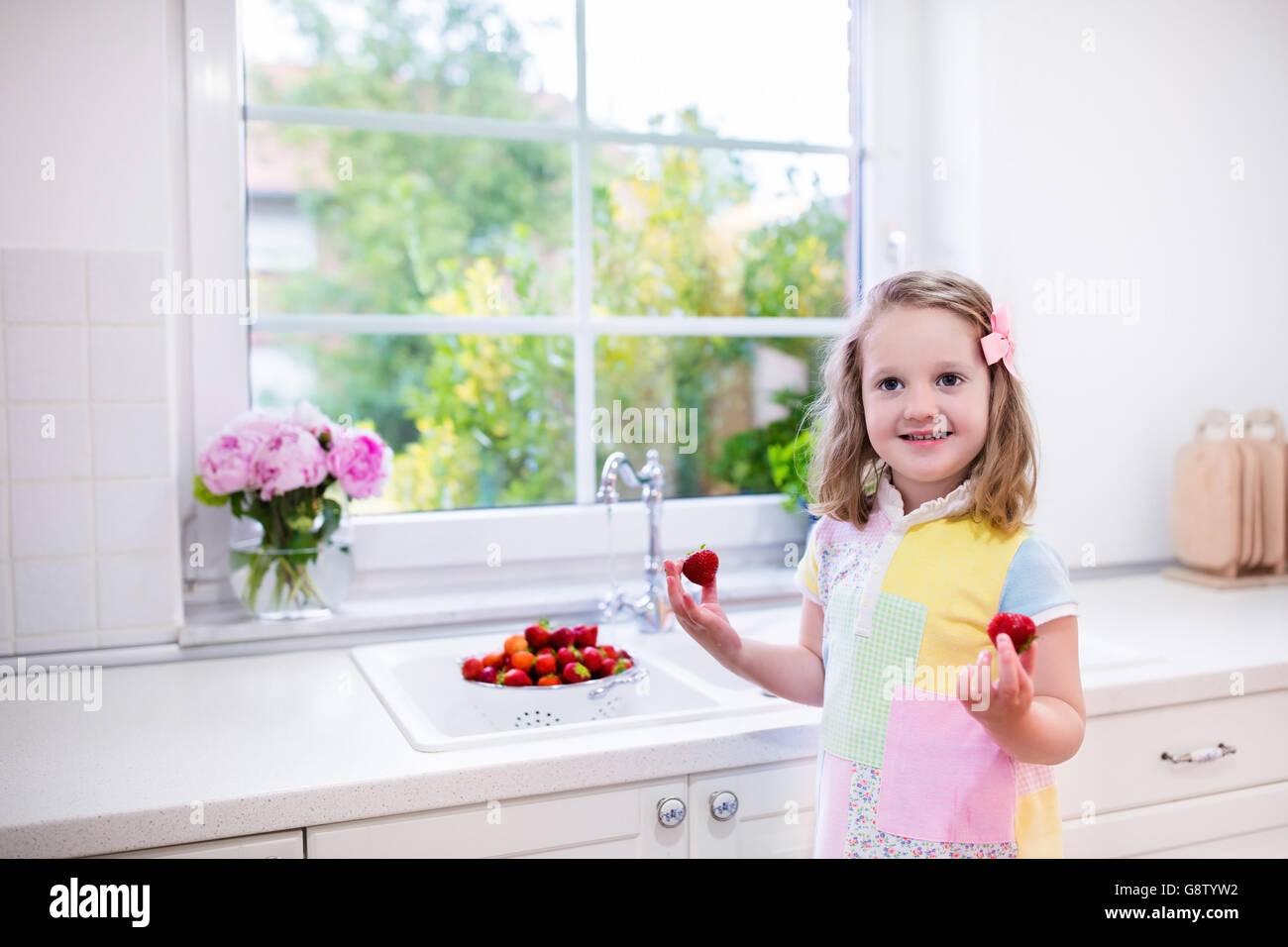 Cute little girl washing fruit in kitchen sink. Child eating strawberry ...
