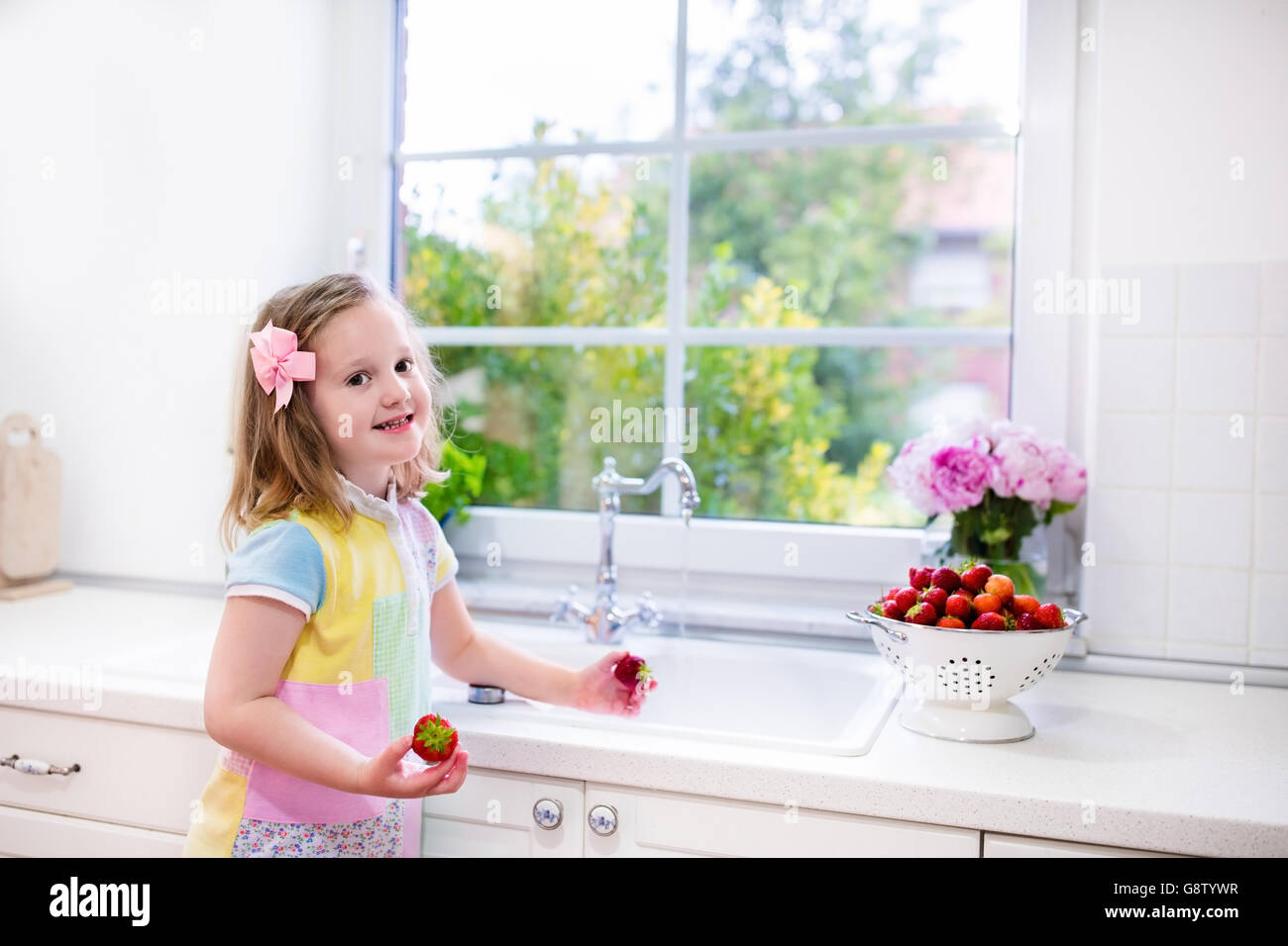 Cute little girl washing fruit in kitchen sink. Child eating strawberry ...
