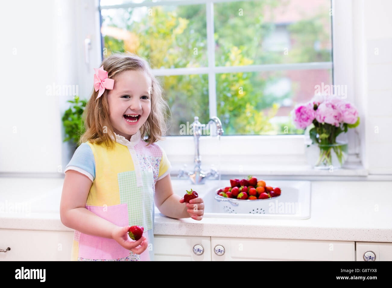 Cute little girl washing fruit in kitchen sink. Child eating strawberry ...