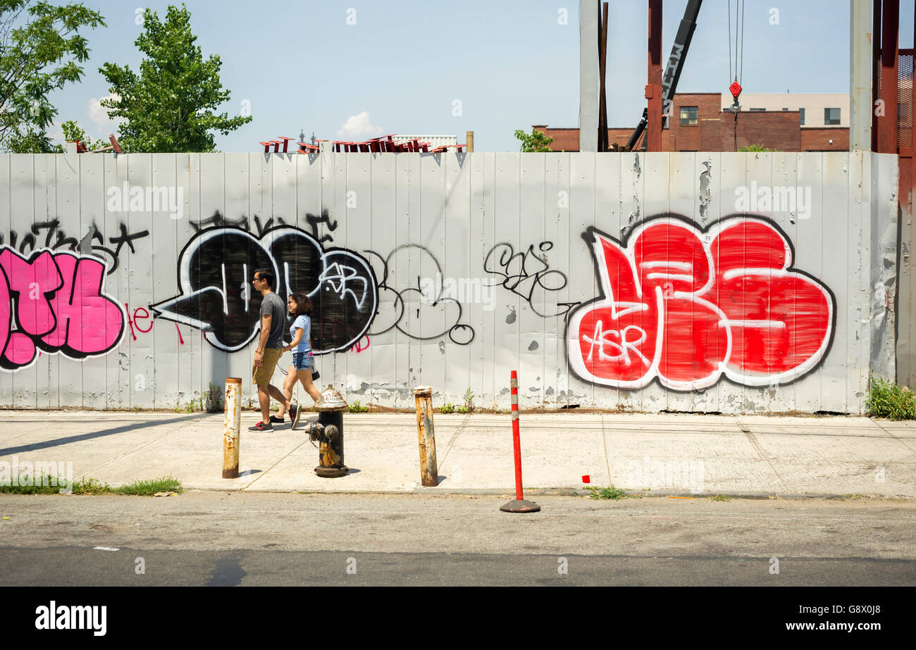 Couple walks past graffitied wall in Long Island City in the borough of ...