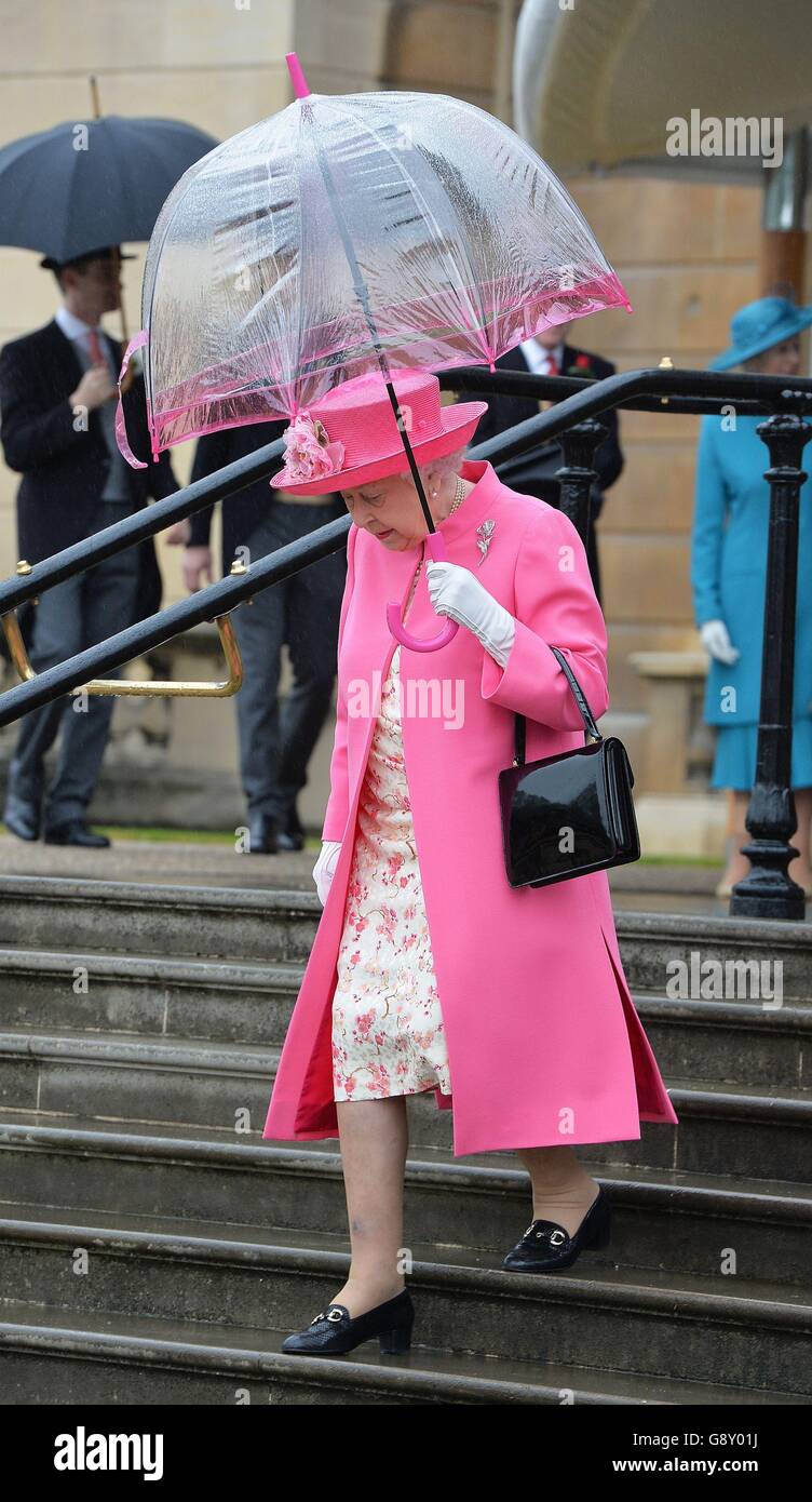 Queen Elizabeth II shelters from the rain under an umbrella as she ...
