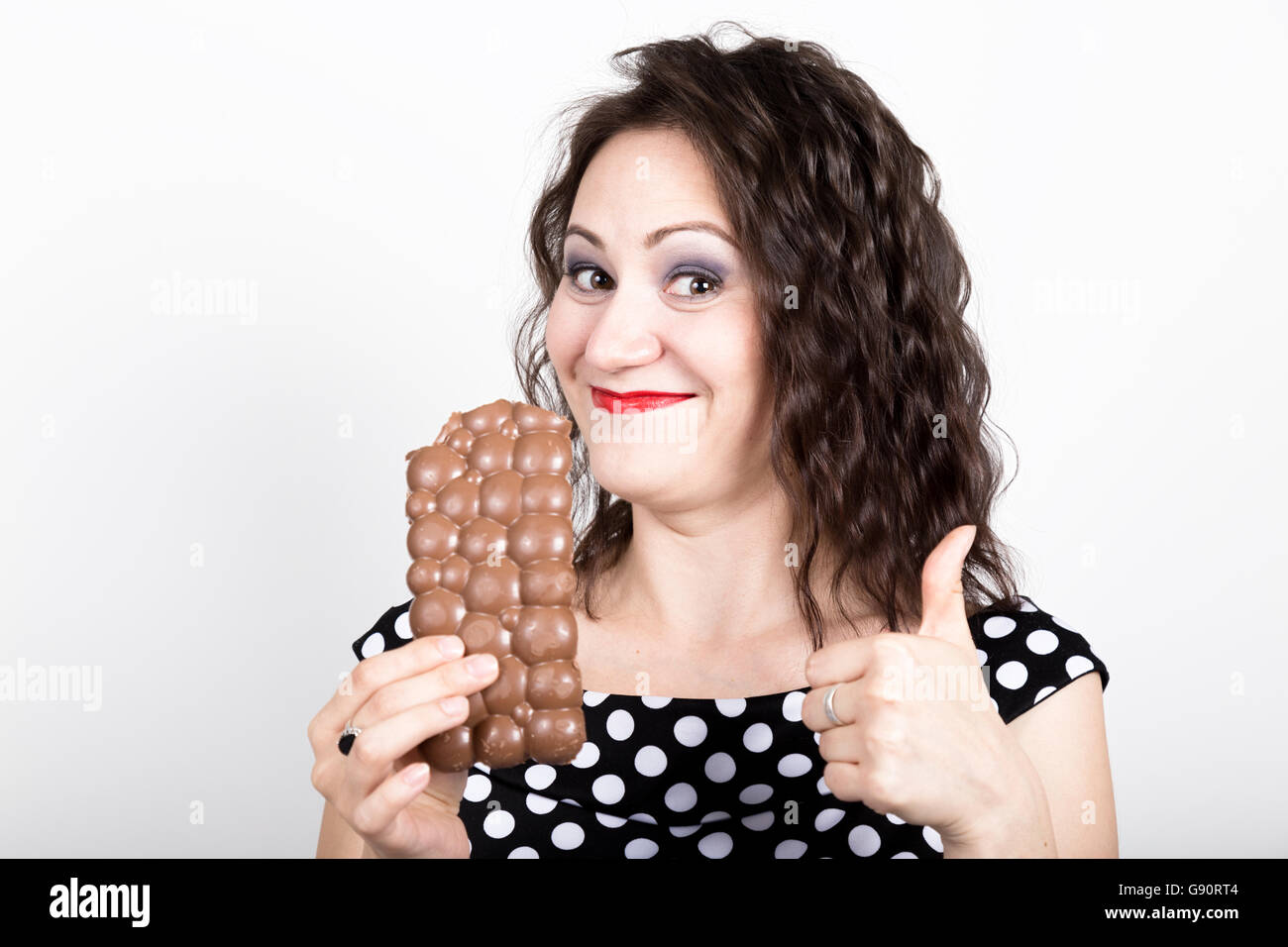 Beautiful young woman eating a chocolate bar, wears a dress with polka ...