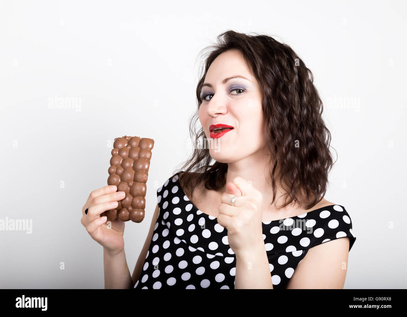 Beautiful young woman eating a chocolate bar, wears a dress with polka ...