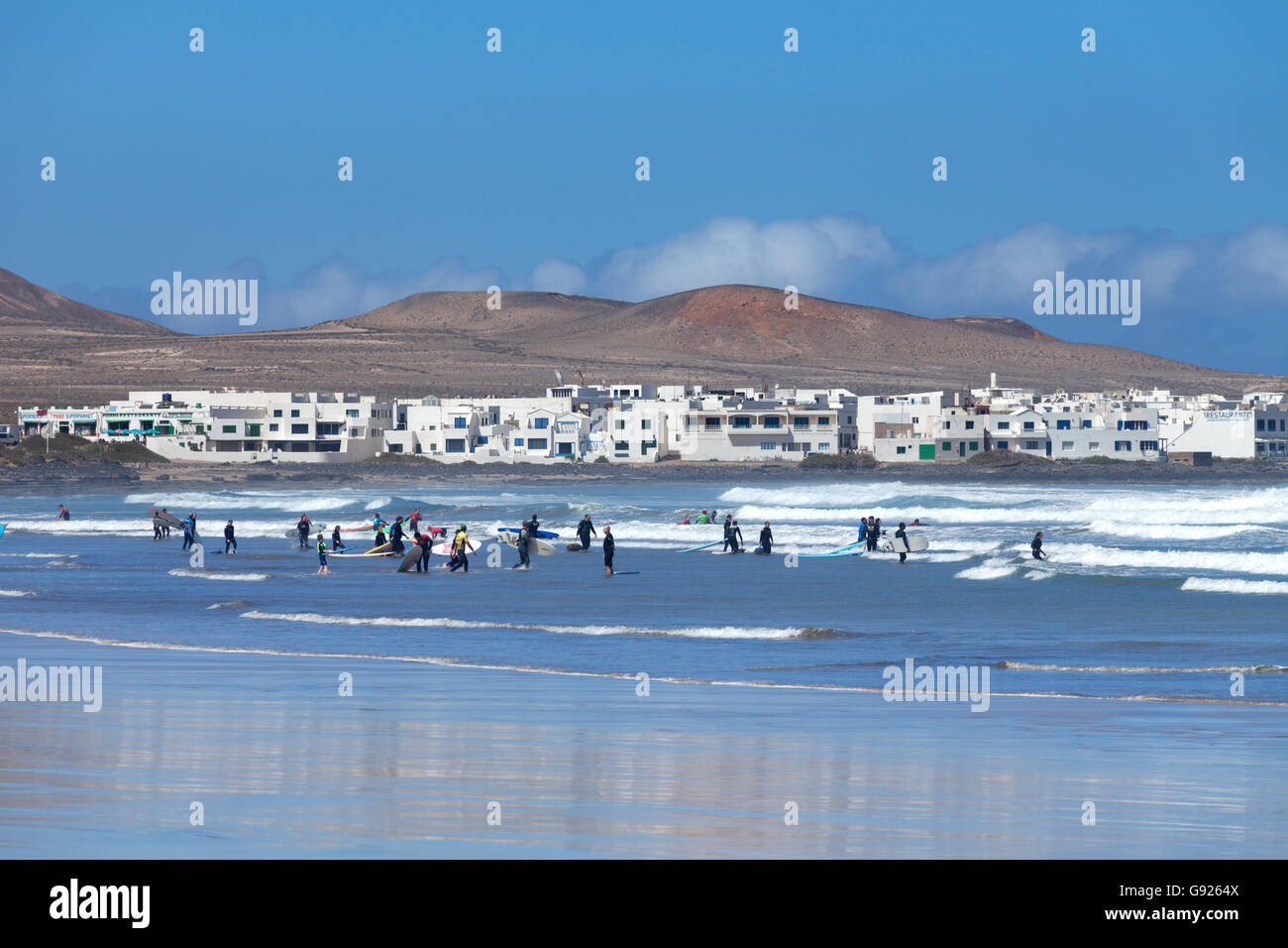 Surfers on the beach Playa de Famara looking towards Caleta de Famara ...