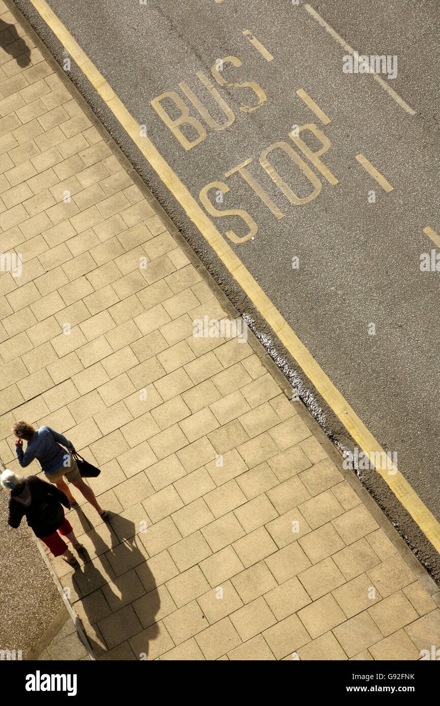 Two people walking alongside an empty bus stop Stock Photo - Alamy