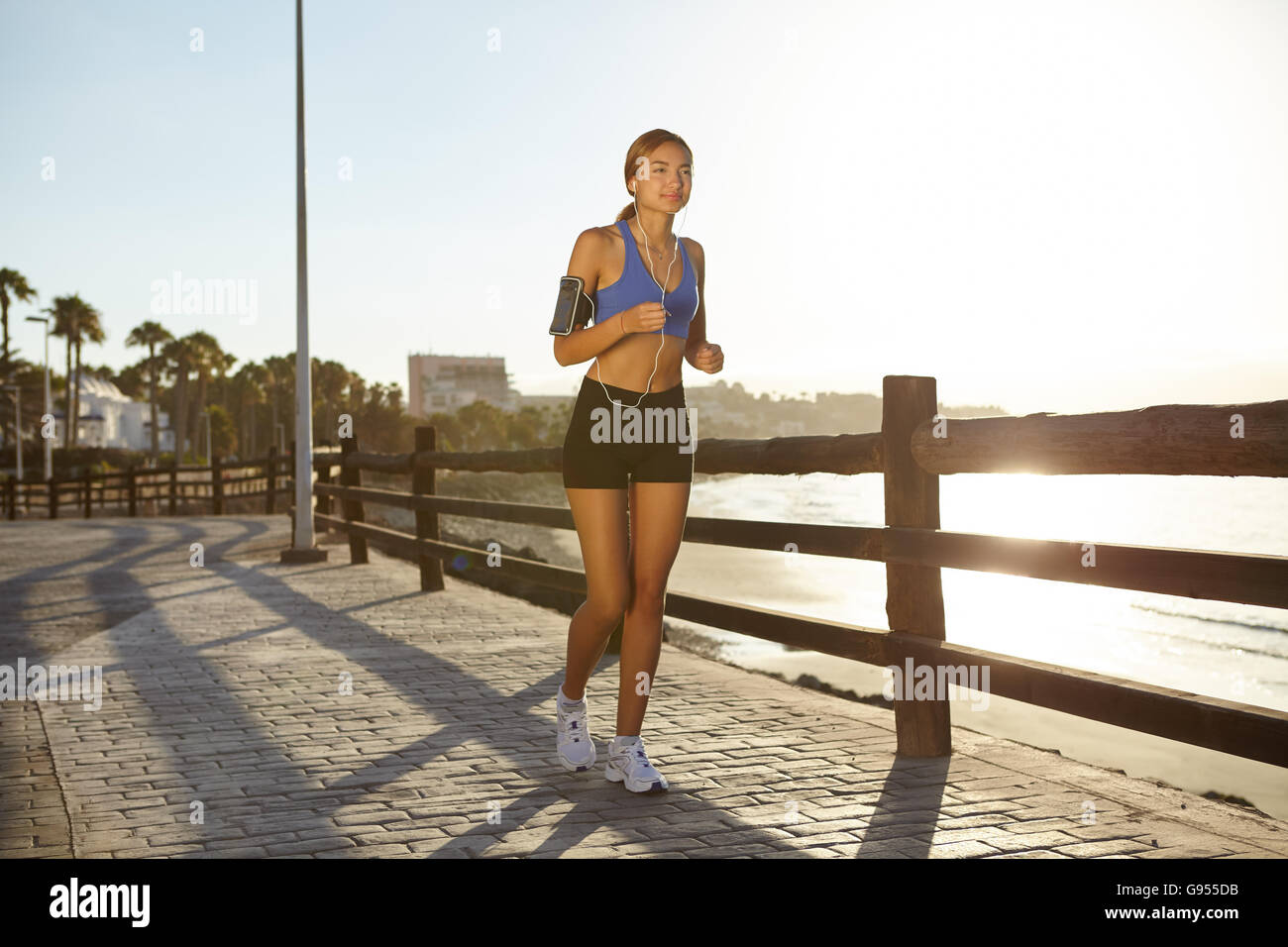 Front view of a young athlete jogging on the beach shore in summertime ...