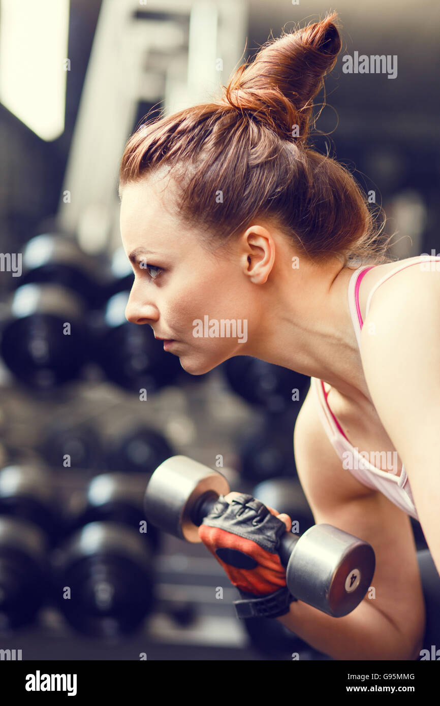 Young confident woman doing biceps curl exercise with dumbbells in ...