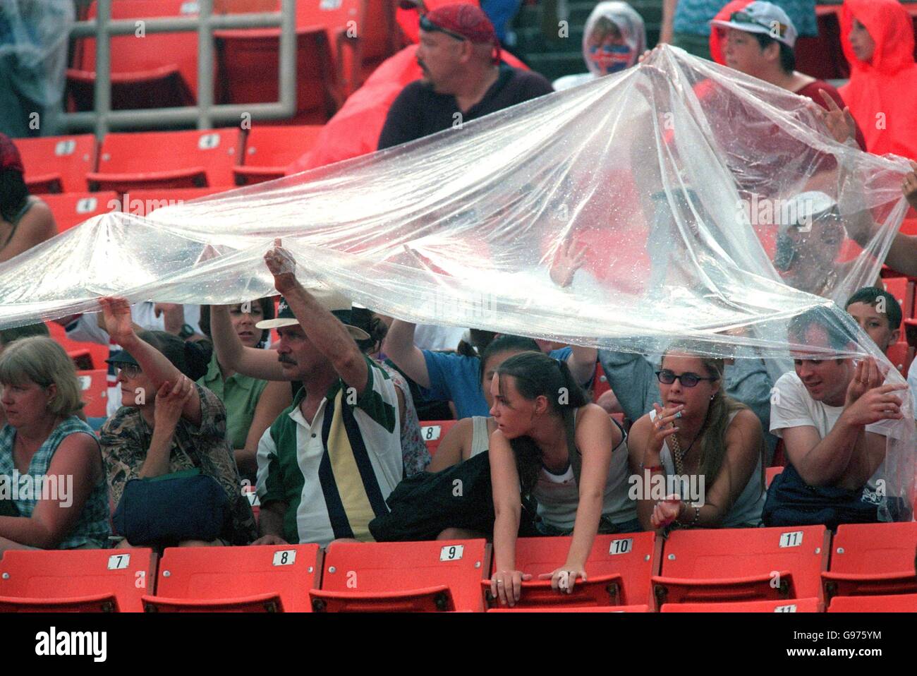 Fans use a plastic sheet to keep the pouring rain off Stock Photo - Alamy