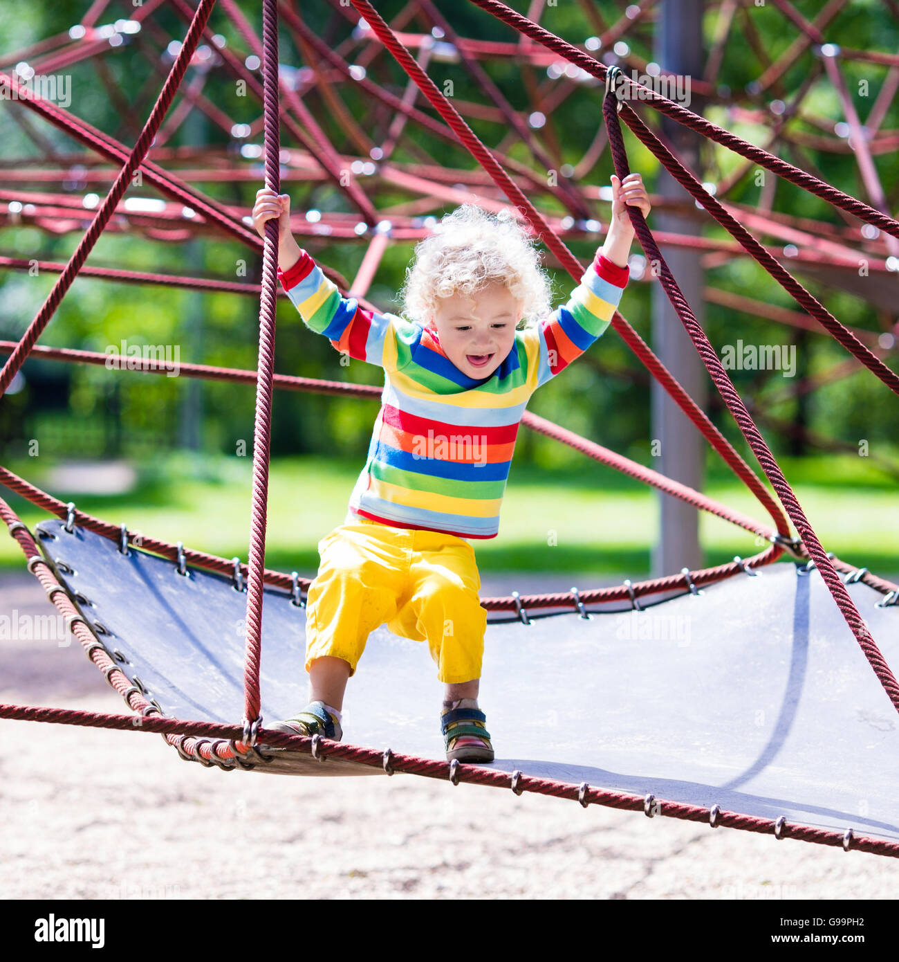 Active little child playing on climbing net and jumping on trampoline ...