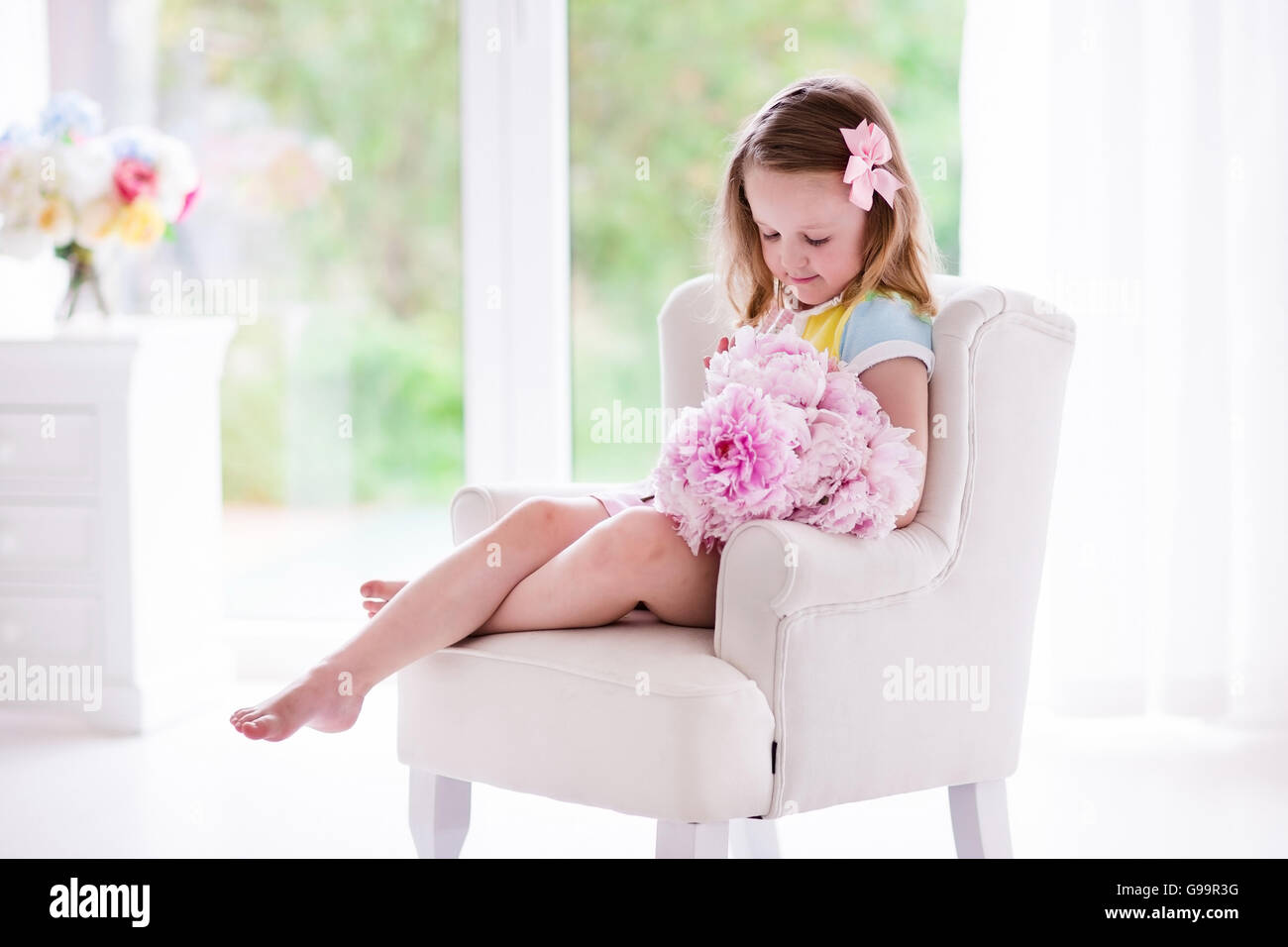 Little girl smelling peony flower bouquet sitting in a white chair in ...