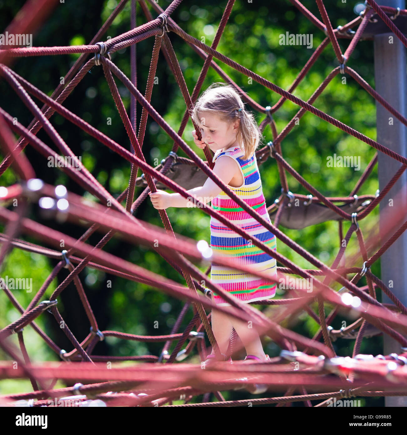Active little child playing on climbing net and jumping on trampoline ...