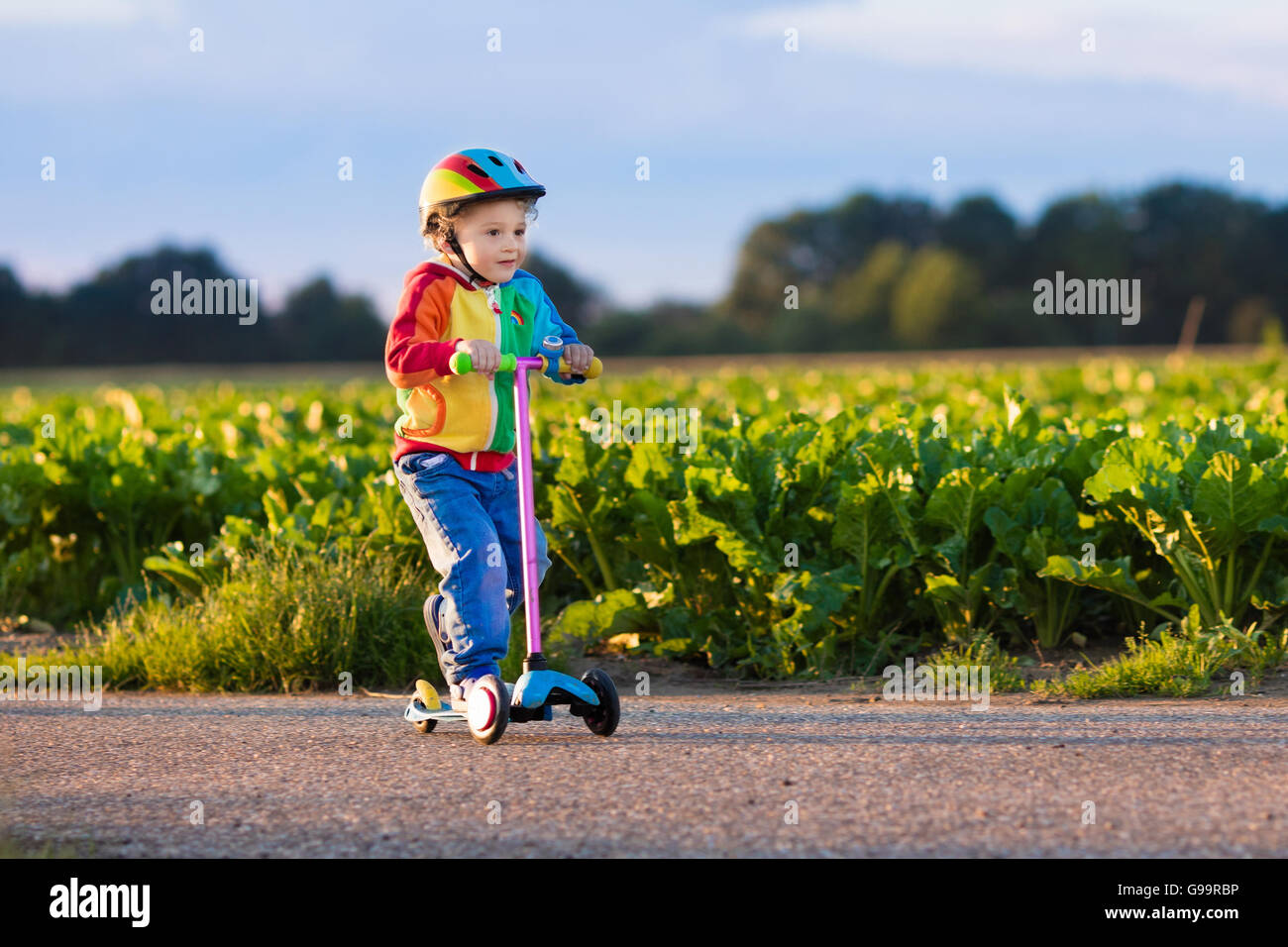Little child learning to ride a scooter in a city park on sunny summer ...