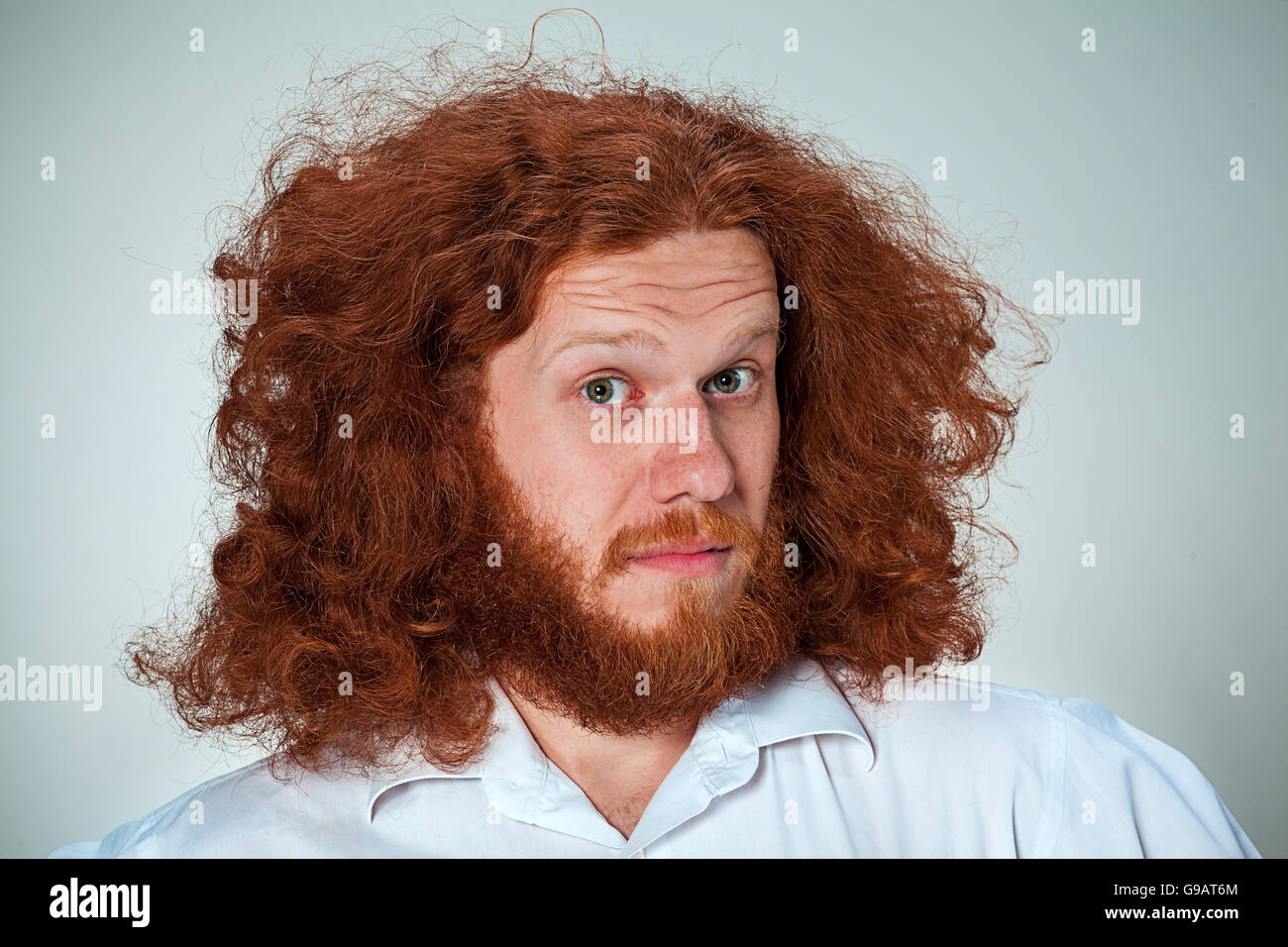 Portrait of young man with long red hair and with shocked facial ...