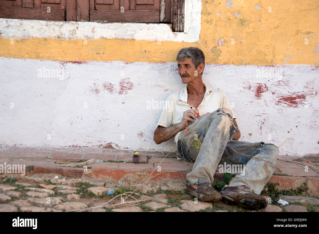 A man sits in the shade on a back street in Trinidad Cuba mending his ...