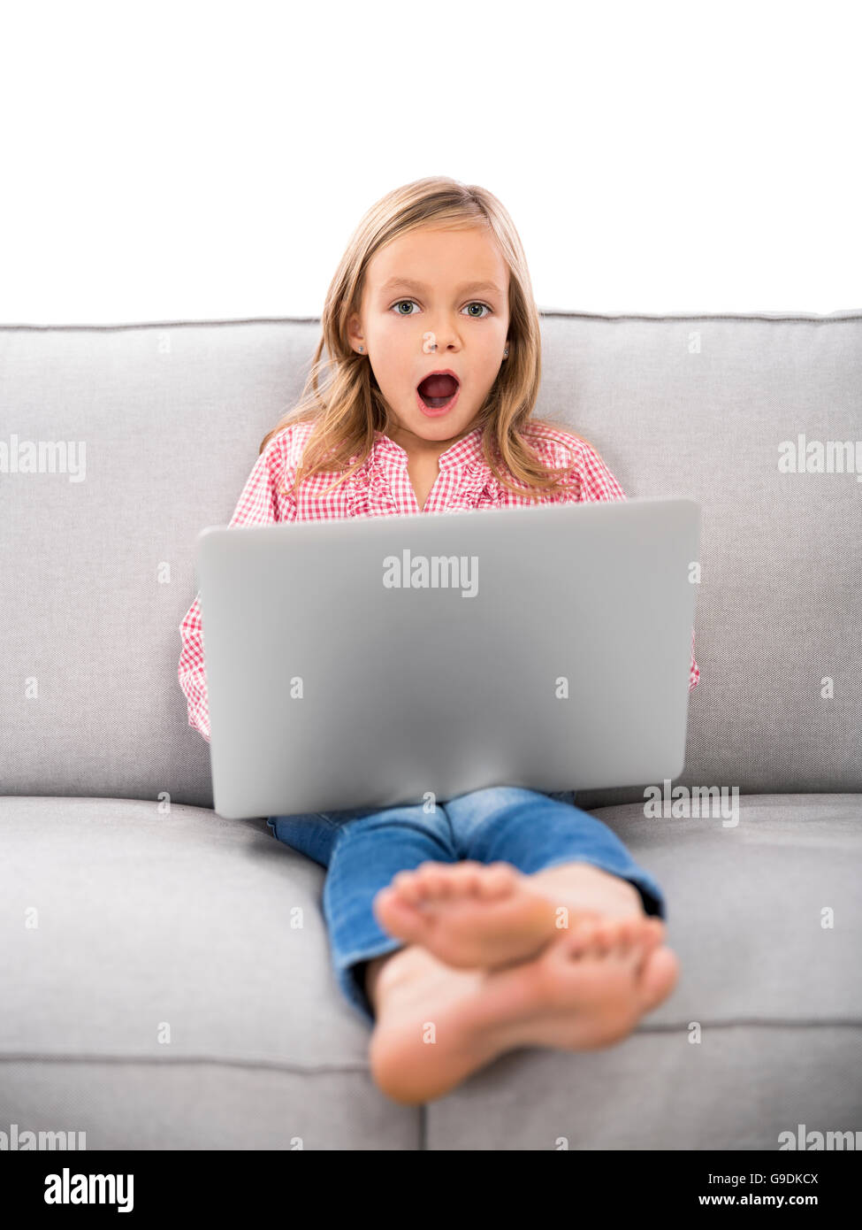 Happy little girl sitting on a couch and working a laptop Stock Photo ...