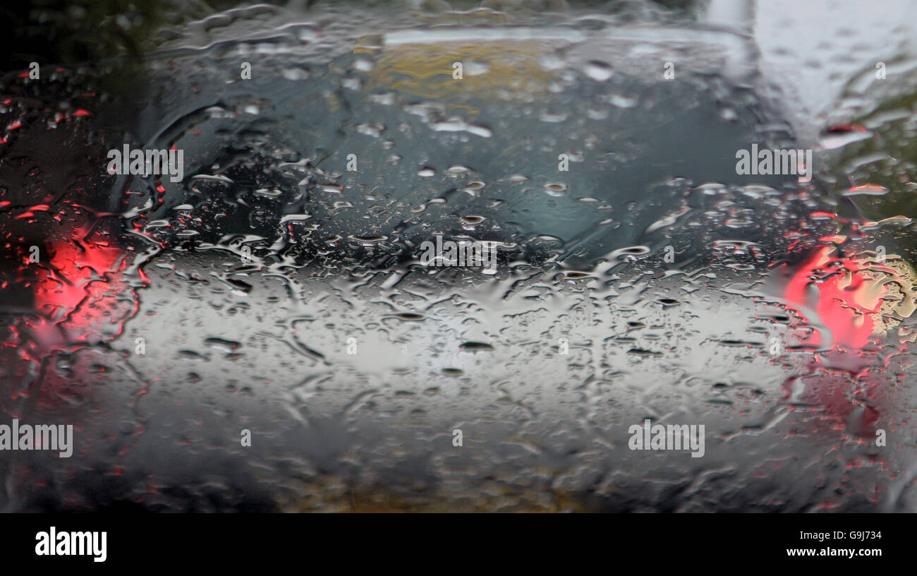 Heavy rainfall on the windscreen of a car with another cars breaklights ...