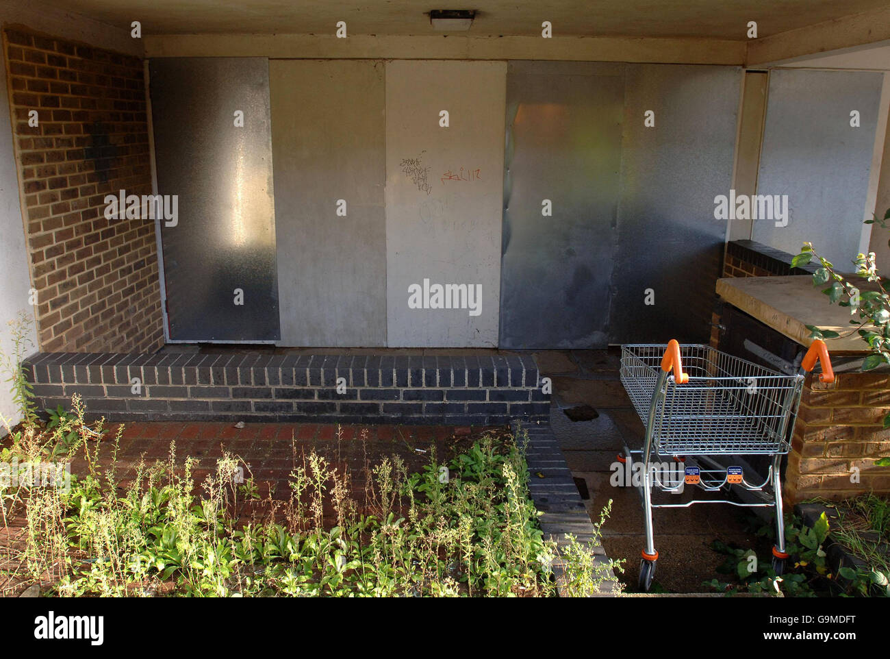 View of a derelict flat with boarded-up windows and a shopping trolley ...