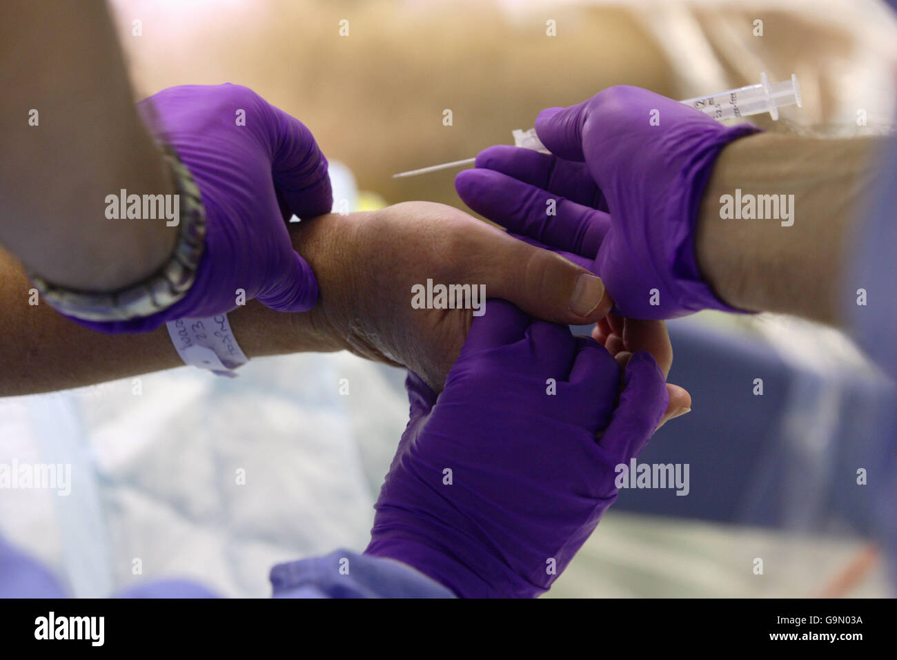 An anaesthetist inserts an arterial line to monitor a patient's blood ...