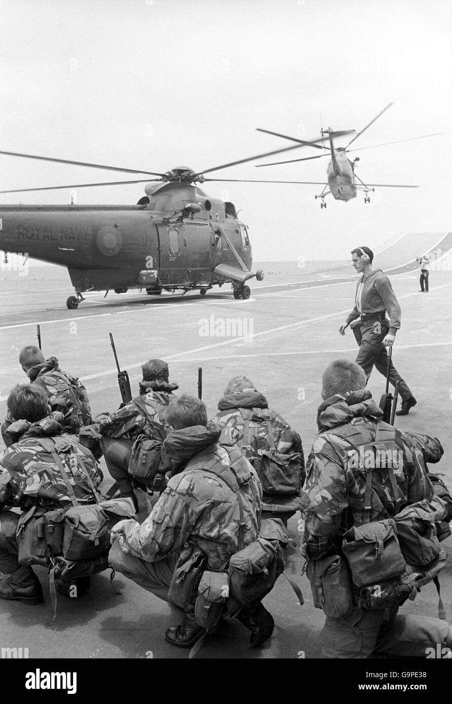 Marines crouching on the flight deck of HMS Hermes as Sea King ...