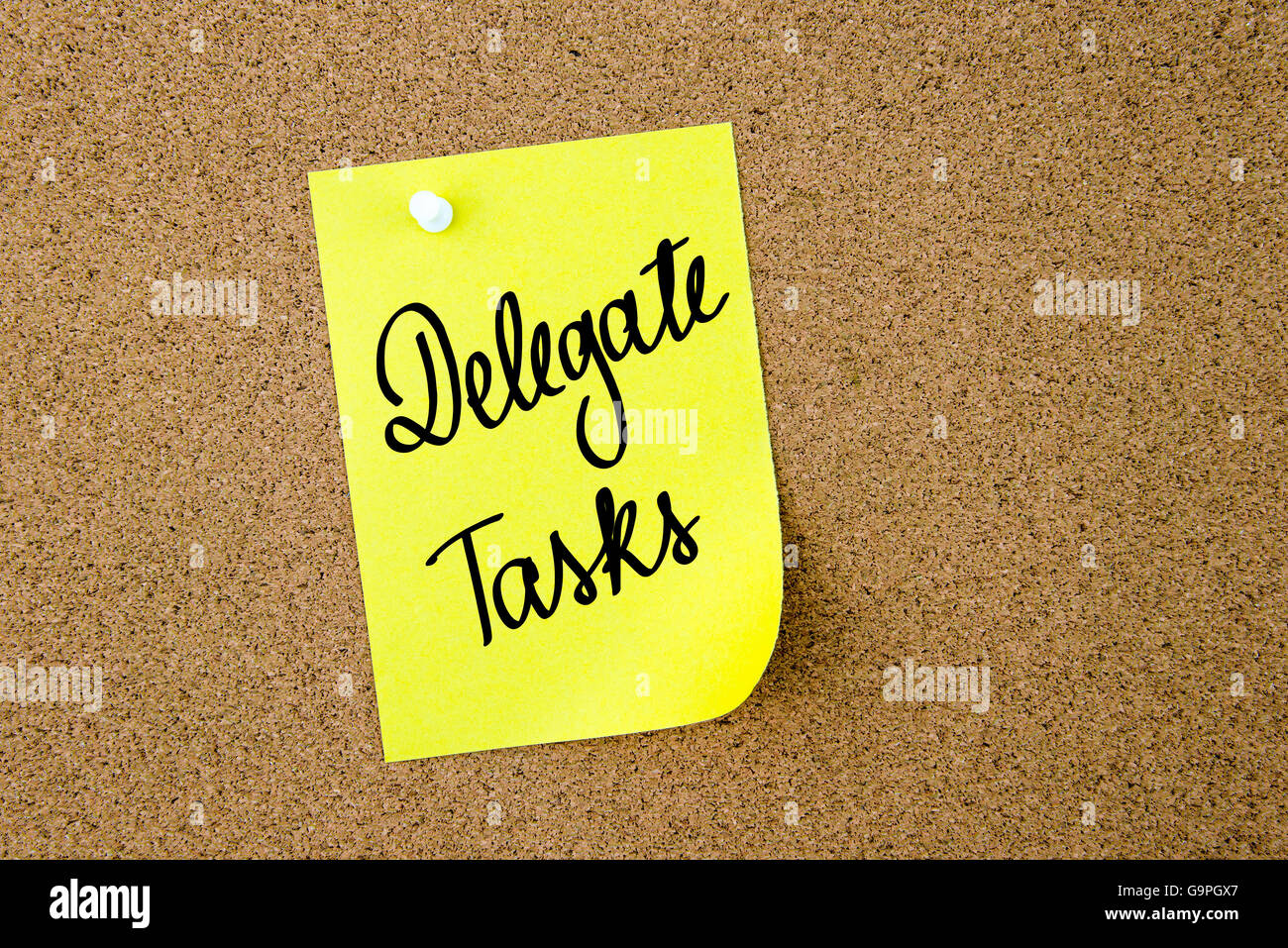 Delegate Tasks written on yellow paper note pinned on cork board with ...