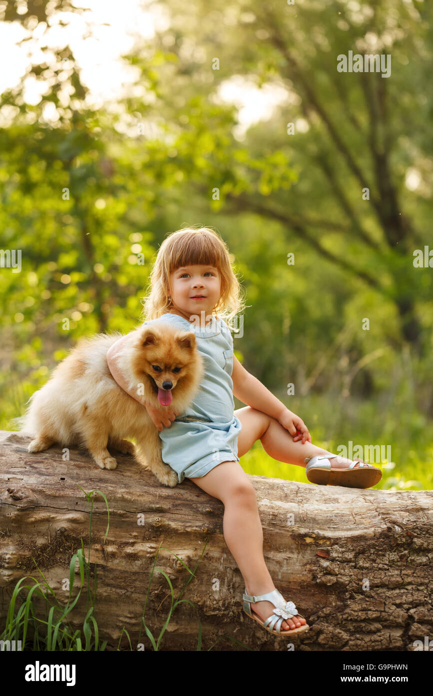 Little girl and pets. The girl and a dog sitting on a fallen tree ...