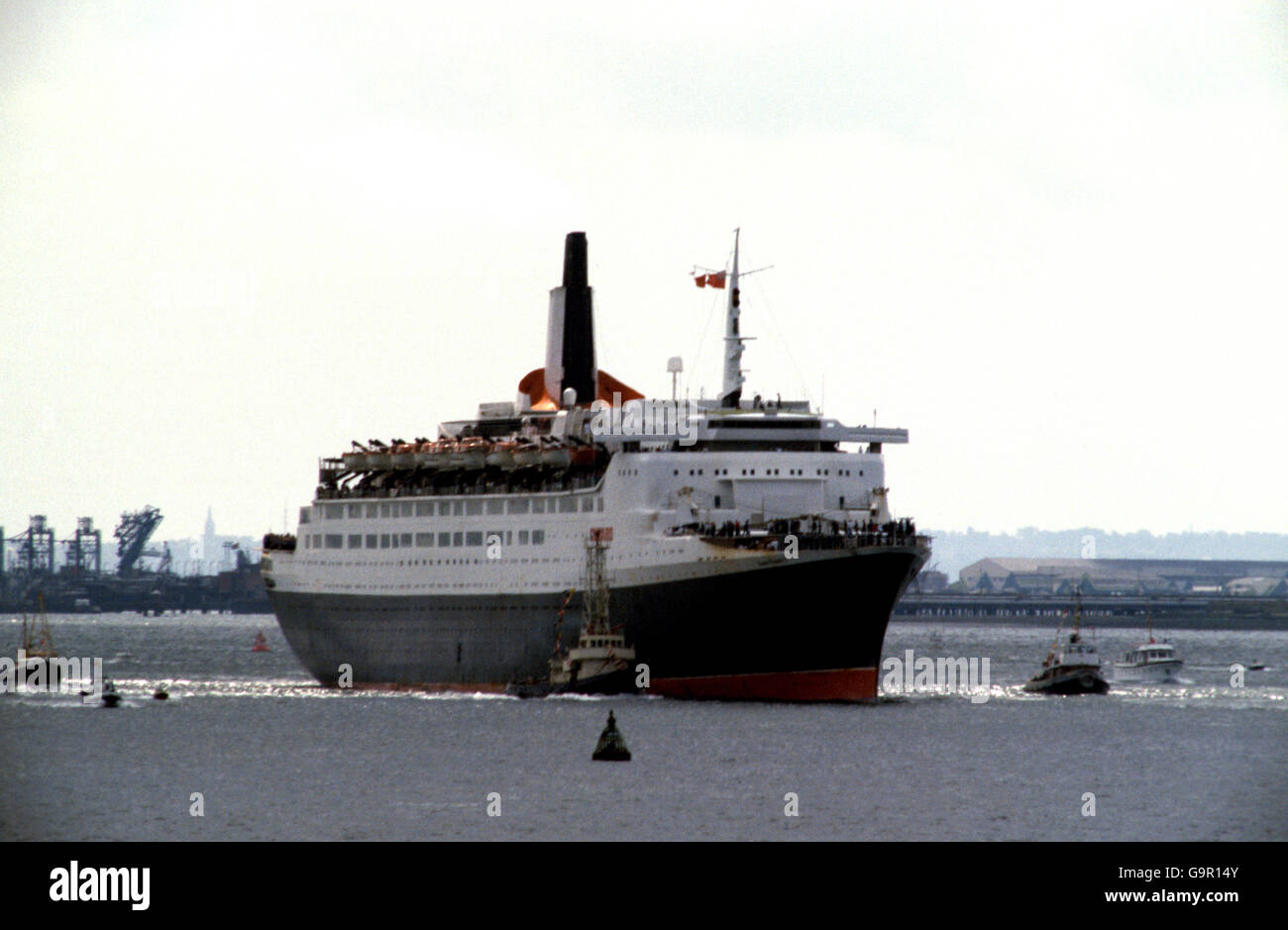 Surrounded by tugs, the QE2 sails up Southampton Water today, with ...