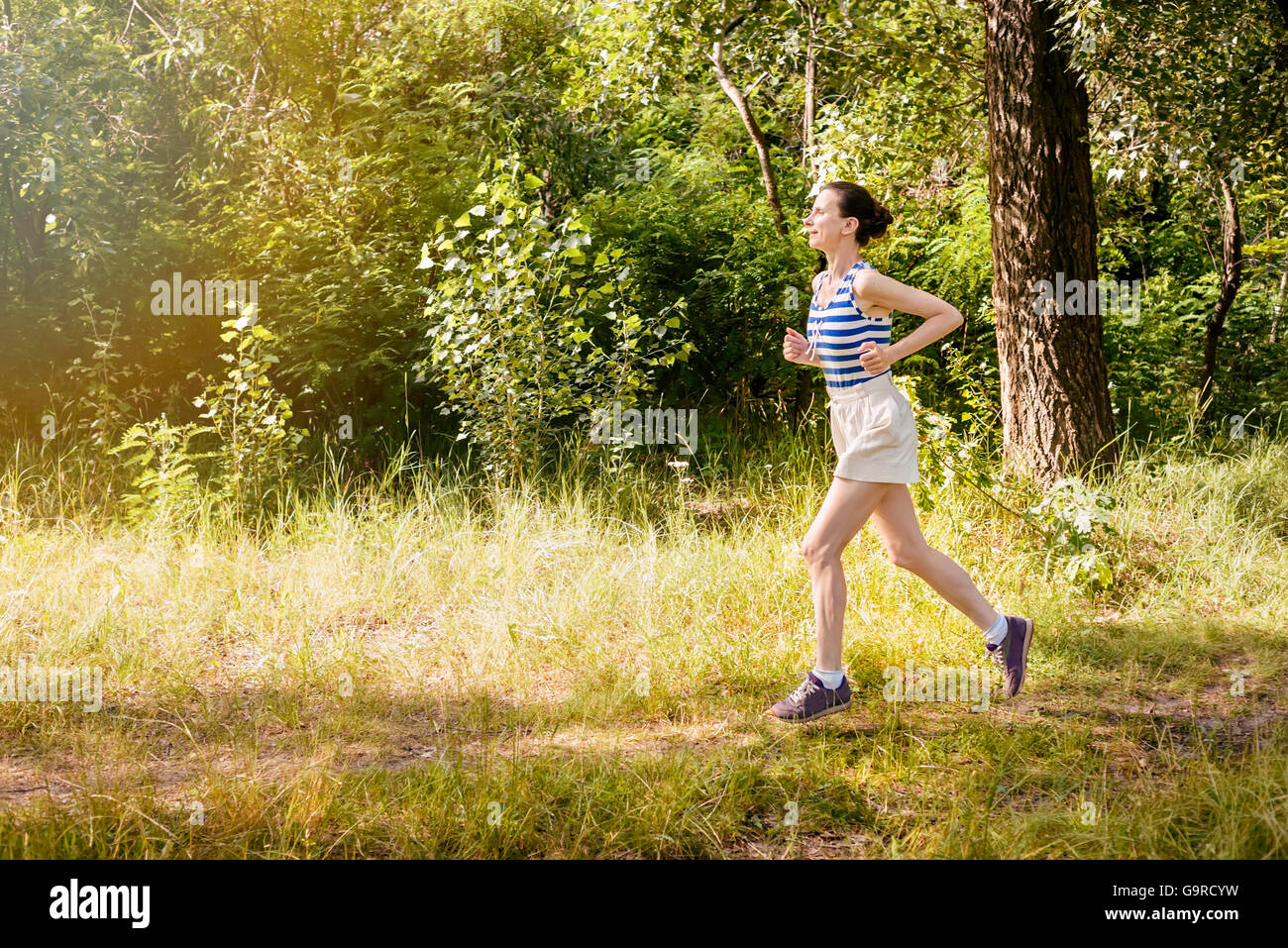 A happy senior woman is running toward the light in the forest during a ...