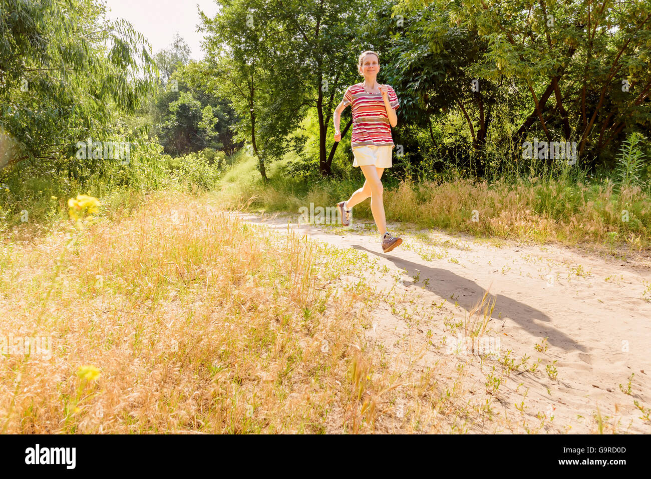 A happy senior woman is running with the sun in backlight, toward the ...