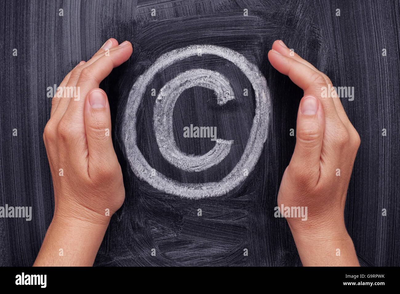 Hands protecting copyright symbol on black chalkboard background. Close ...