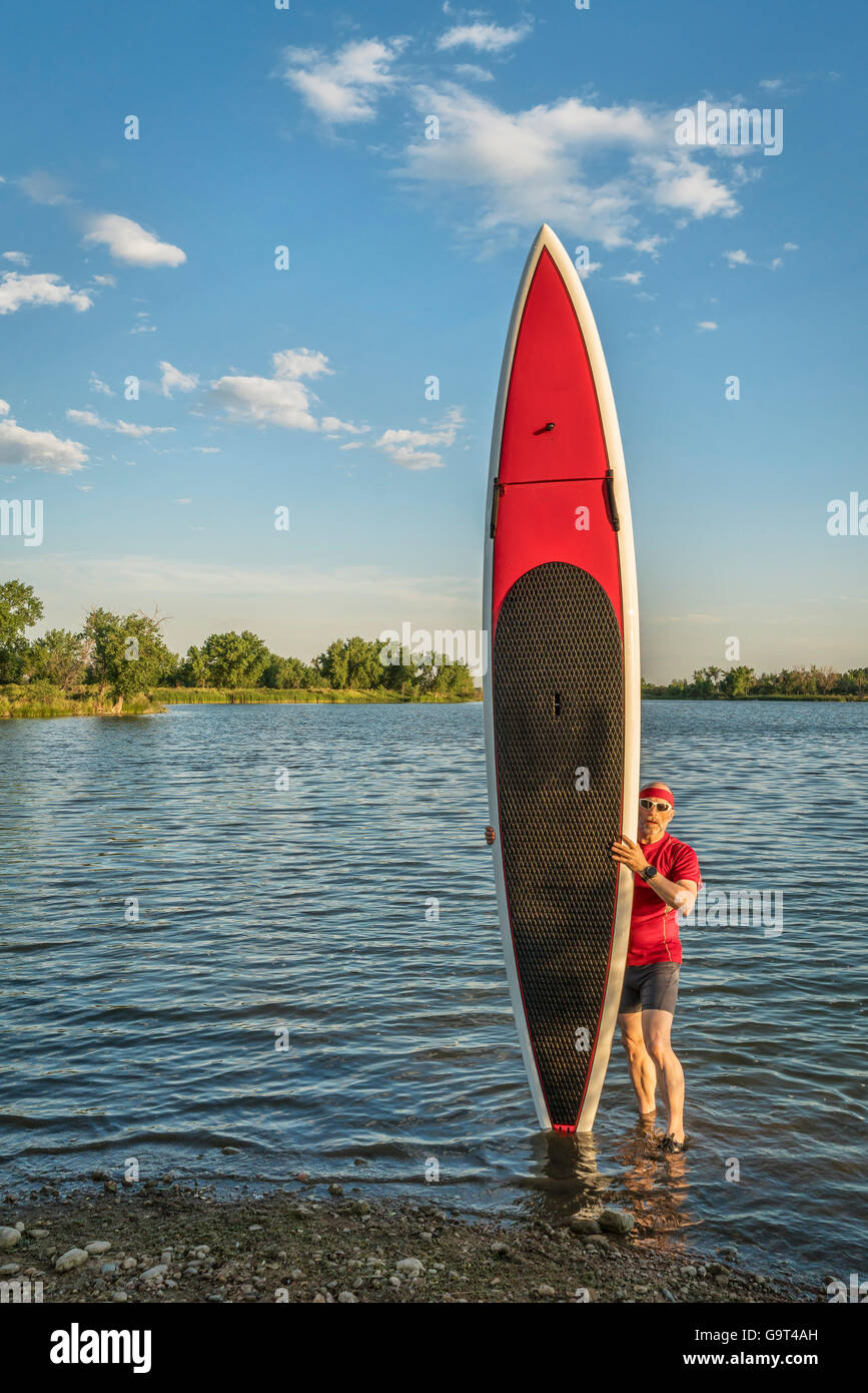 male paddler with his long stand up paddleboard on a lake shore Stock ...