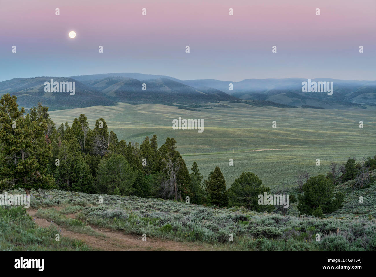 full moon setting at dawn over mountains covered by wildfire smoke ...