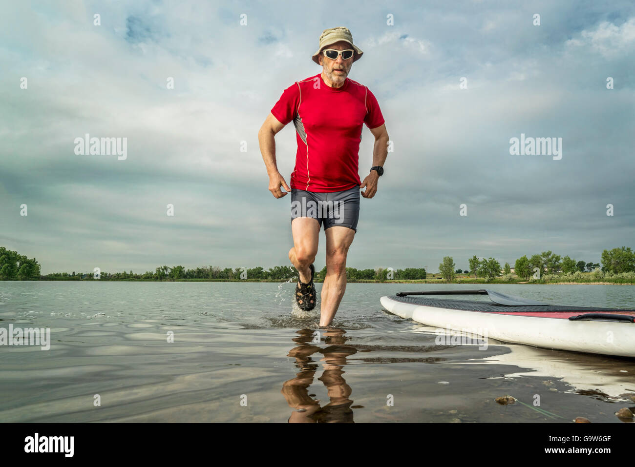 senior paddler with stand up paddleboard on, lake shore in northern ...