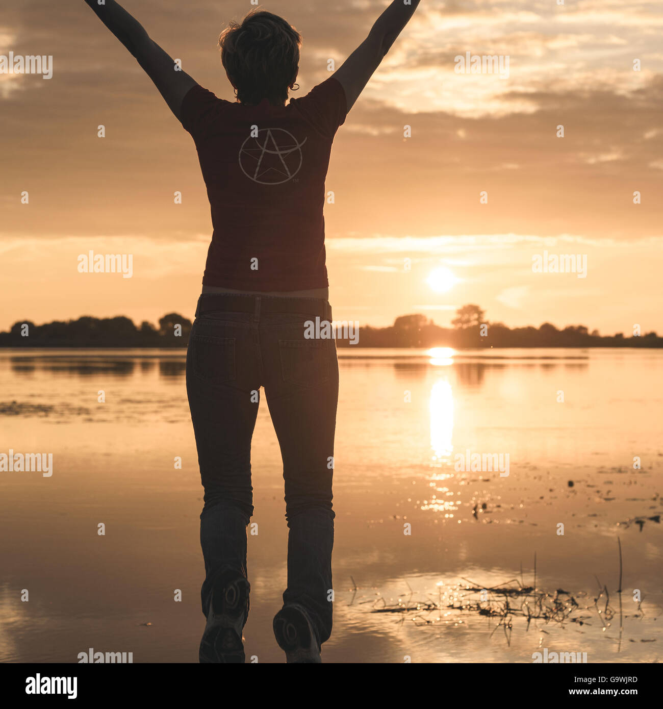 happy young slim woman jumping up on the shore of the lake at sunset ...