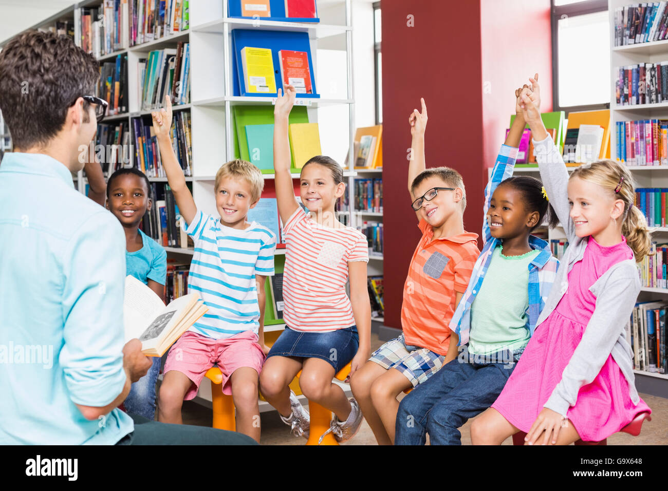 Kids raising their hands in library Stock Photo - Alamy