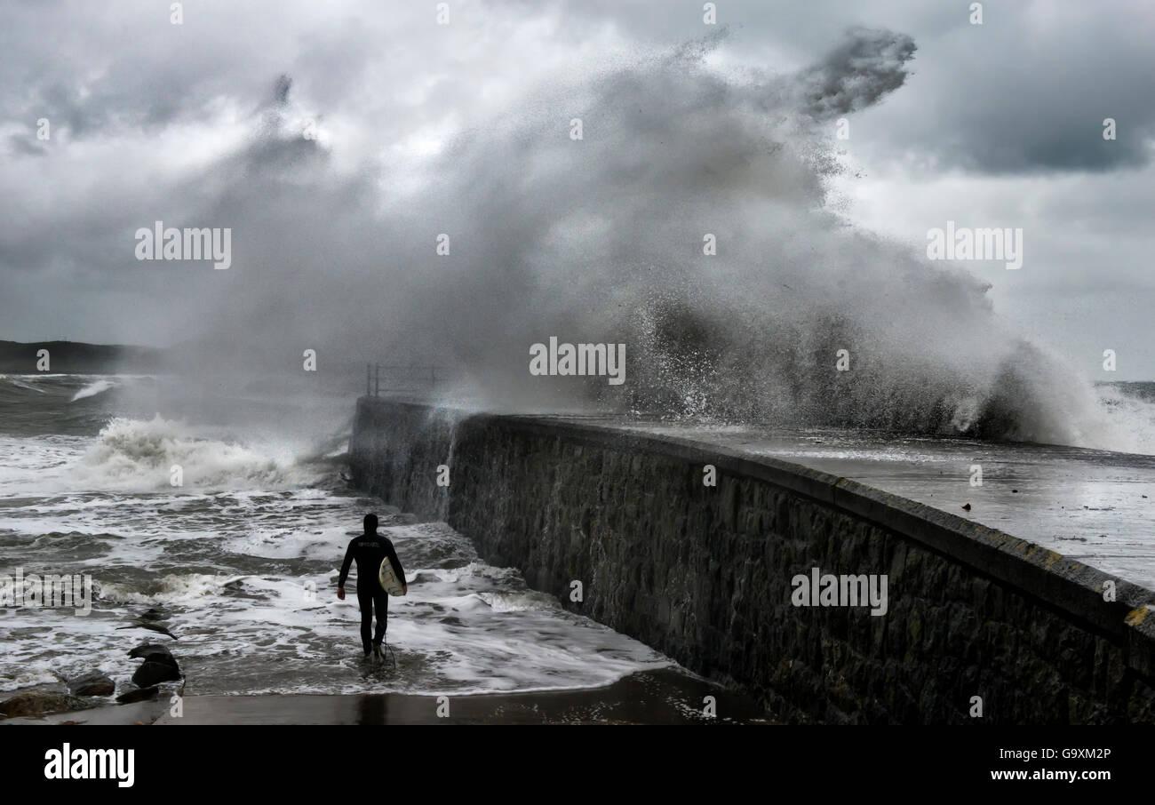 Surfer entering the sea with large waves breaking over the jetty during ...