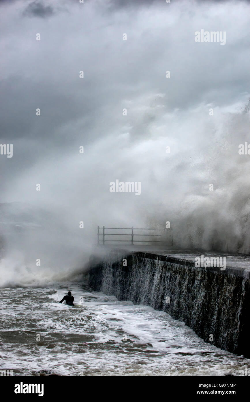 Surfer entering the sea with large waves breaking on the jetty during ...