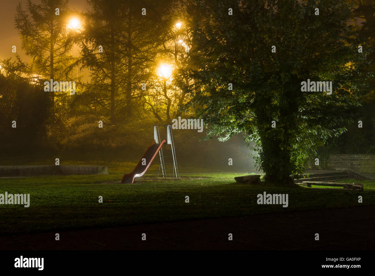 an empty playground with a red slide at night with fog and creepy ...