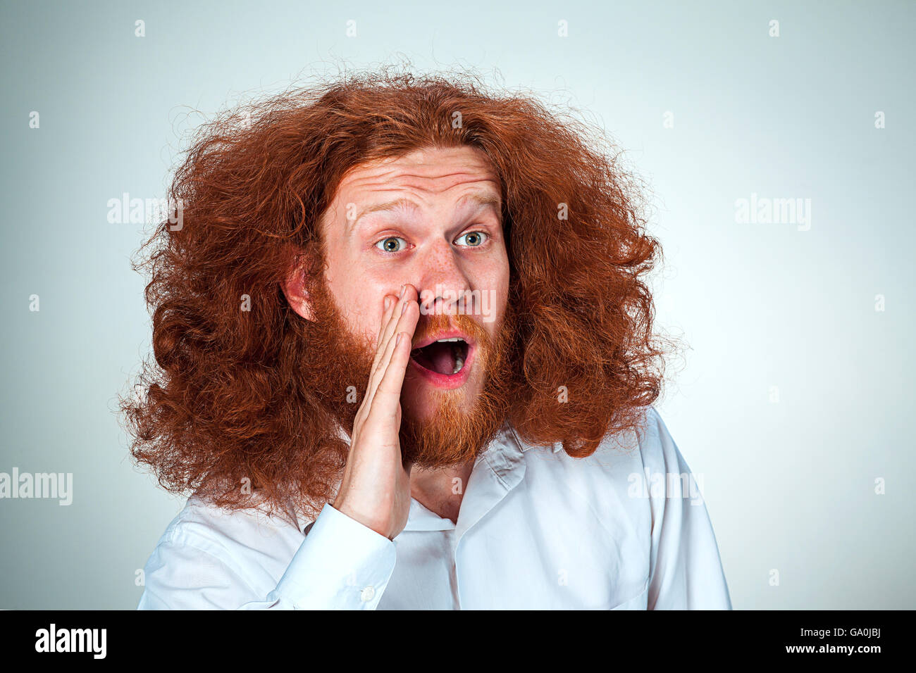 Portrait of screaming young man with long red hair and shocked facial ...