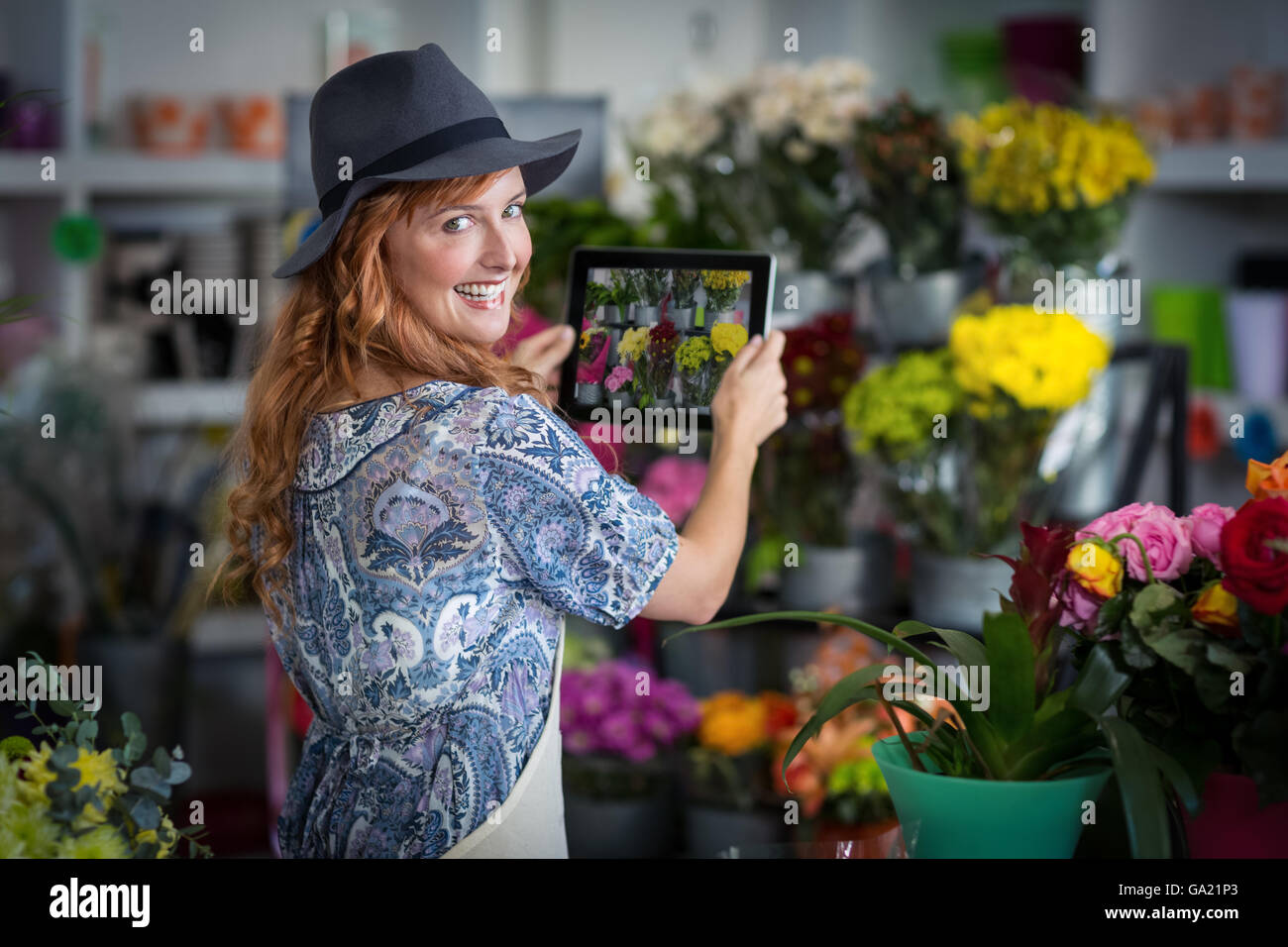 Female florist taking photograph of flowers from digital tablet in ...