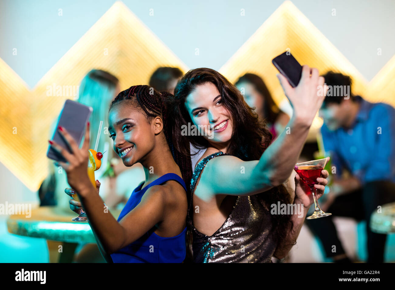 Smiling friends taking a selfie from mobile phone while having cocktail ...