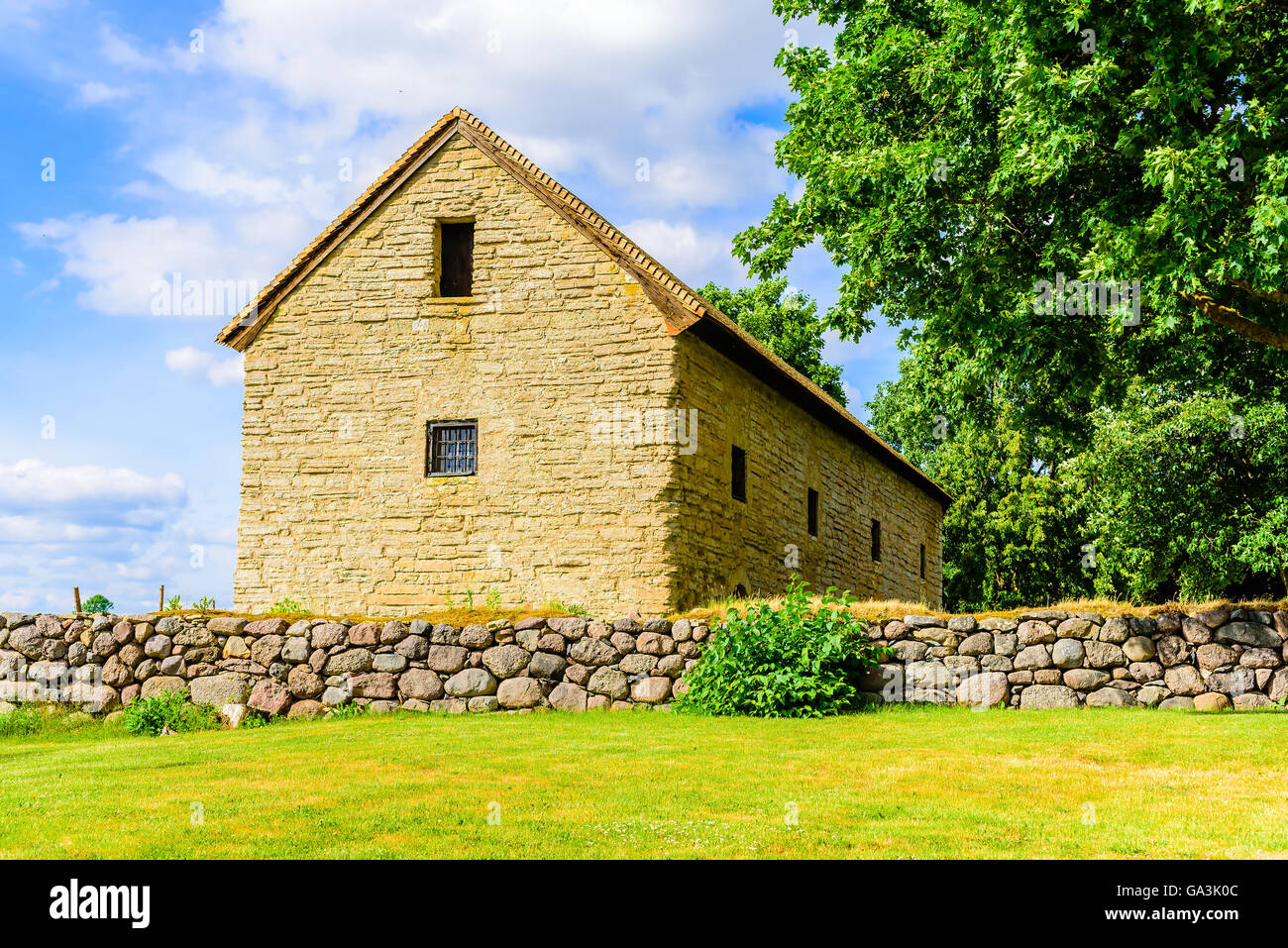 Ancient limestone farm building and granite stone wall beside trees ...