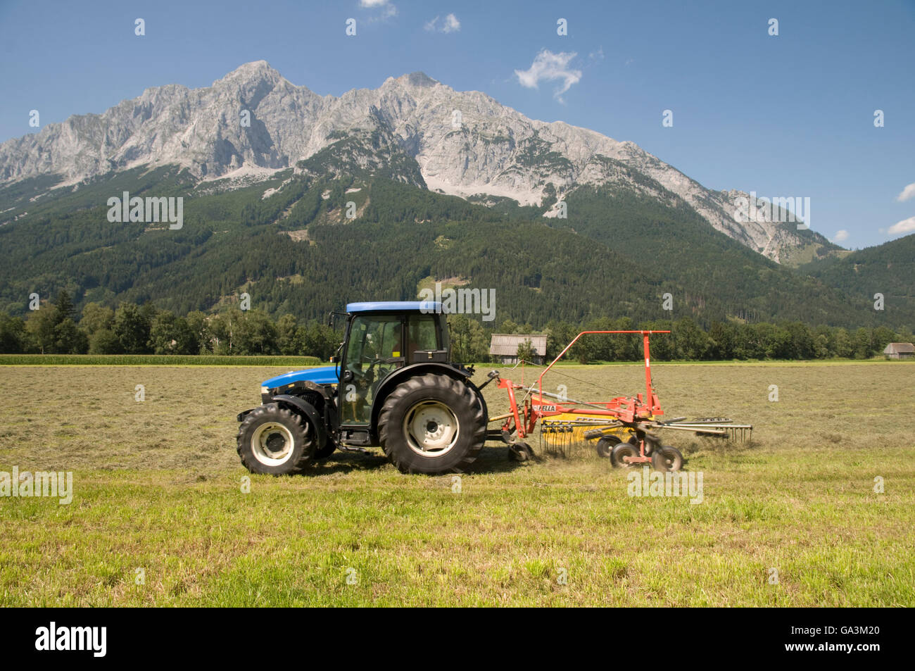Tractor working the fields, behind the Dachsteingebirge mountains ...