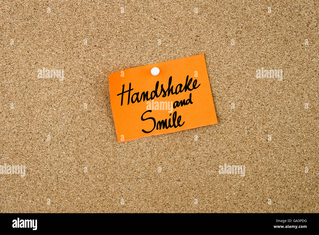 Handshake and Smile written on orange paper note note pinned on cork ...