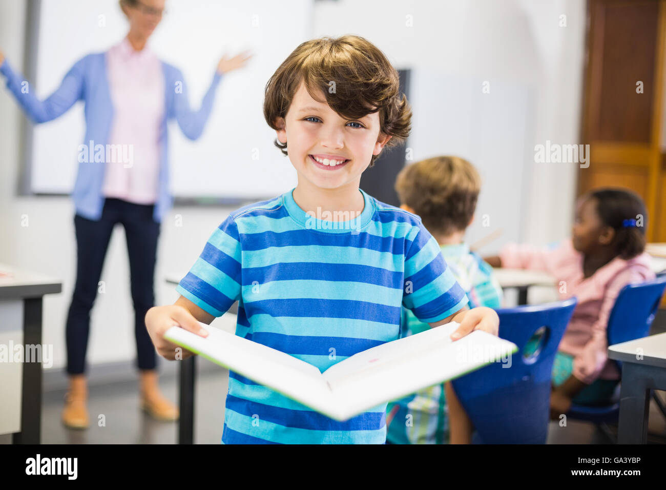Portrait of schoolboy standing with book in classroom Stock Photo - Alamy