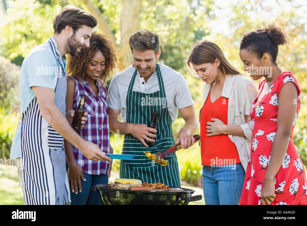 Happy friends preparing a barbecue grill in park Stock Photo - Alamy