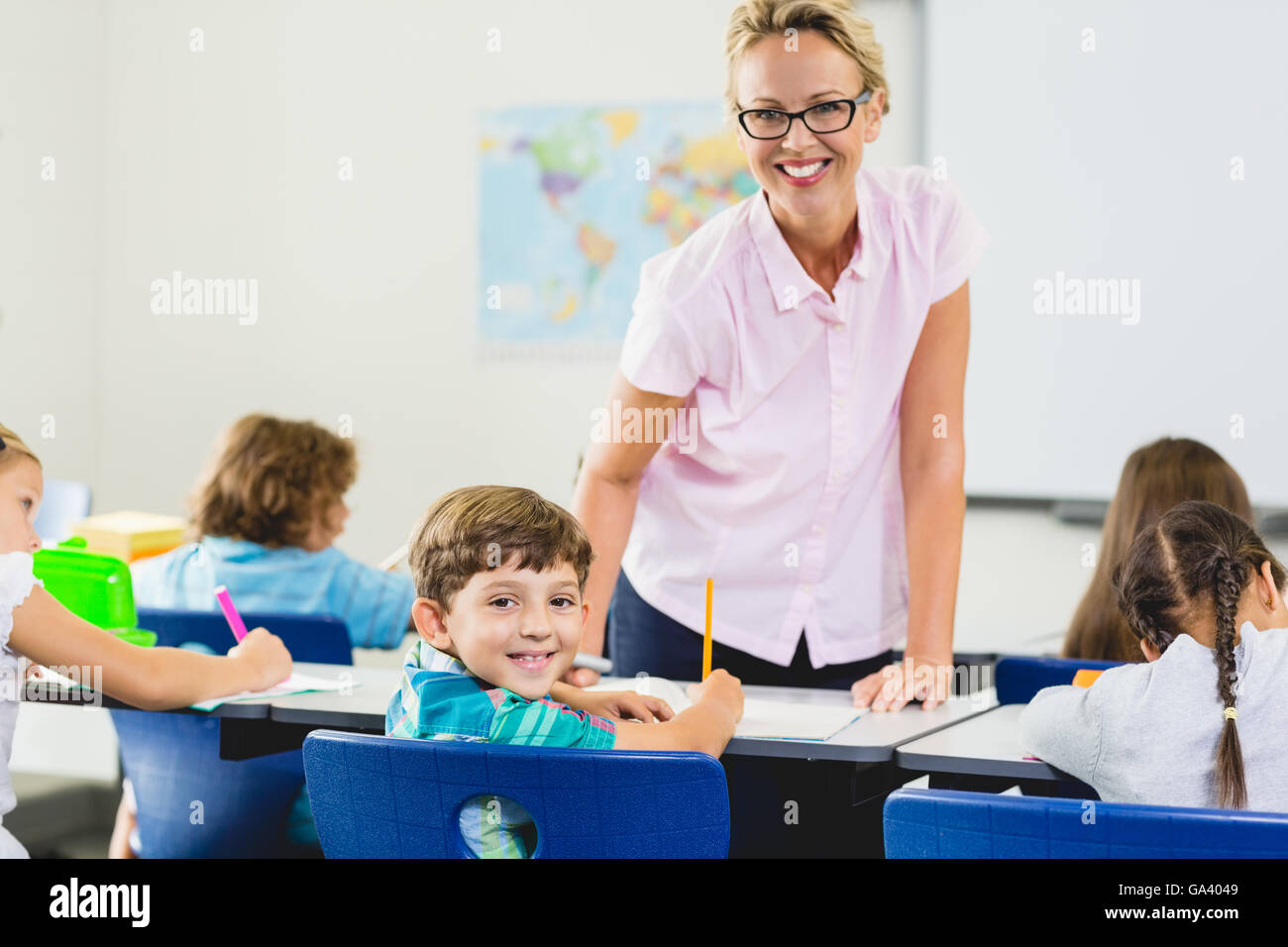 Teacher helping kids with their homework in classroom Stock Photo - Alamy